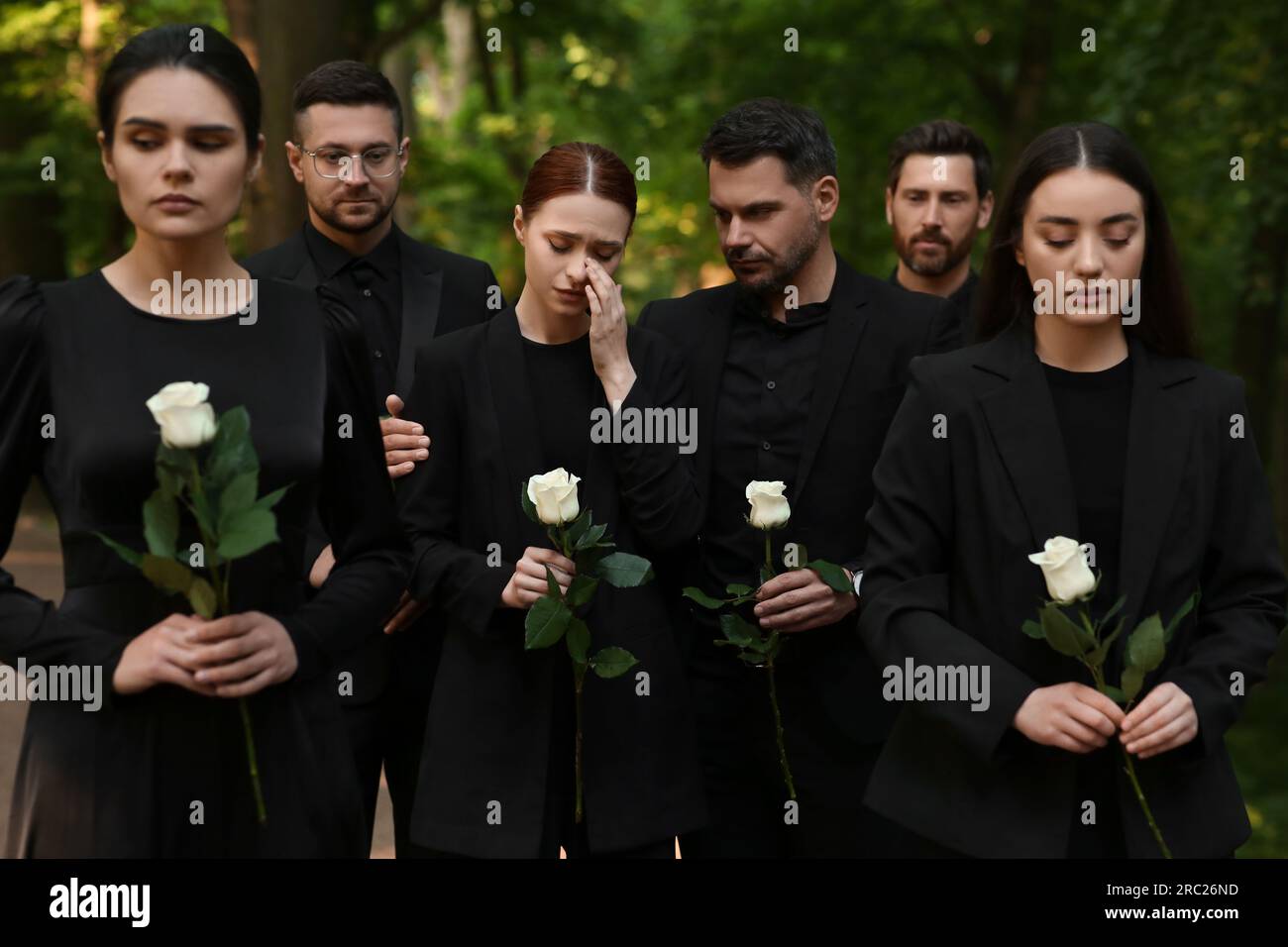 Funeral ceremony. Sad people with white rose flowers mourning outdoors ...