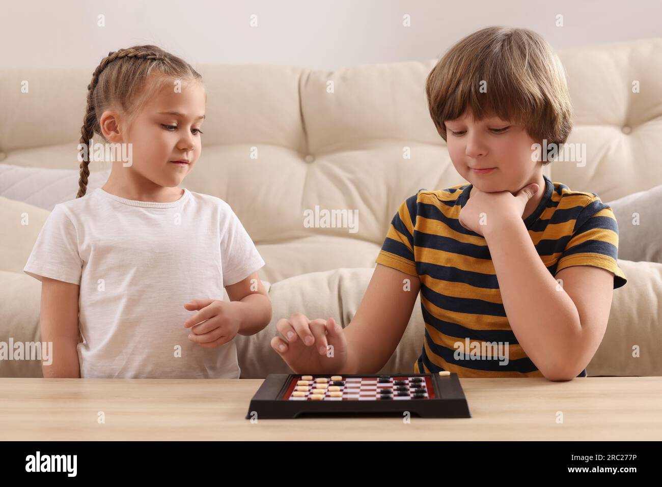 Cute boy playing checkers with little girl at light wooden table in ...