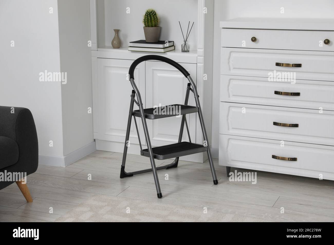 Metal folding ladder near chest of drawers and shelf with accessories ...