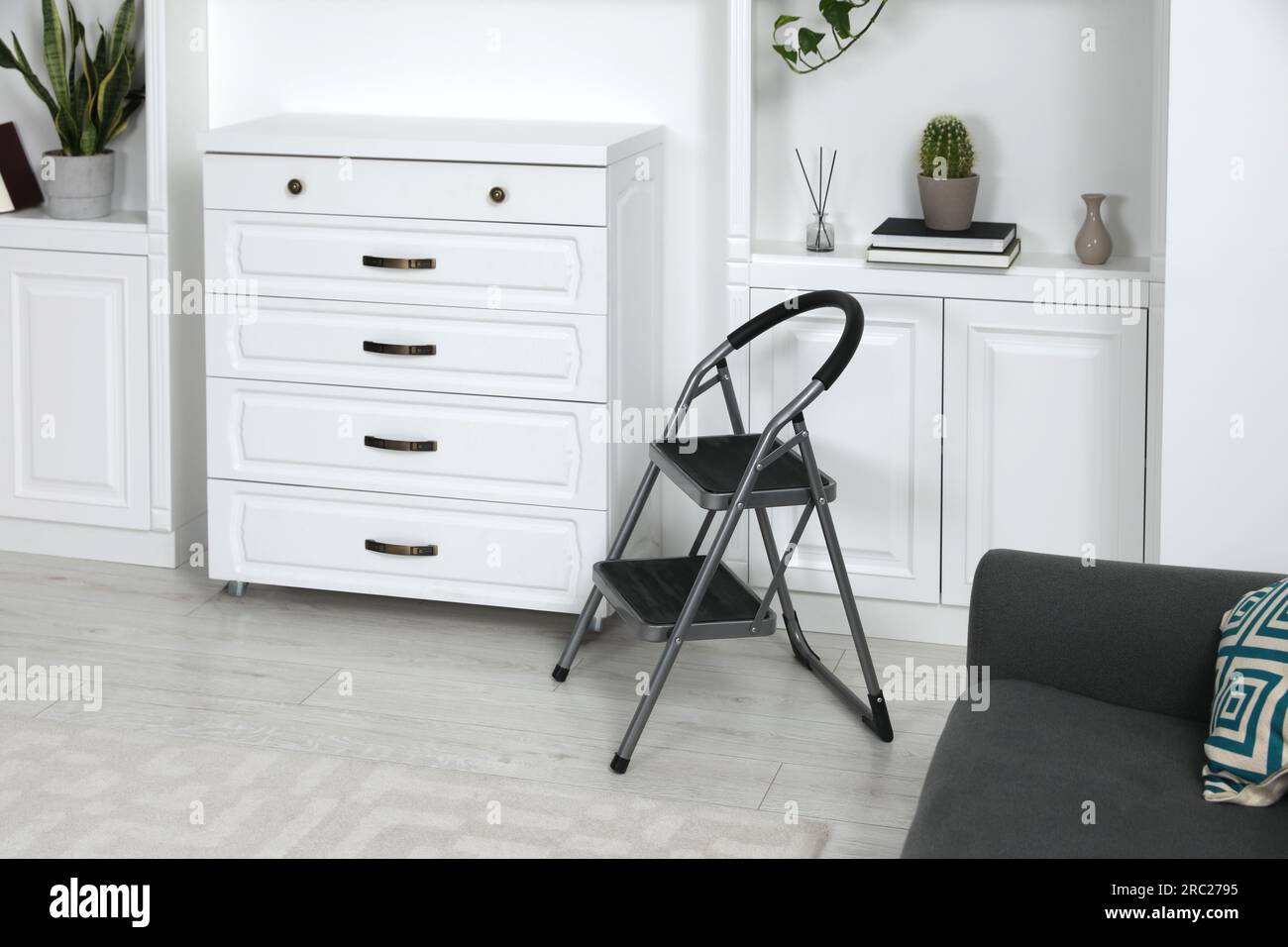Metal folding ladder near chest of drawers and shelves with accessories ...