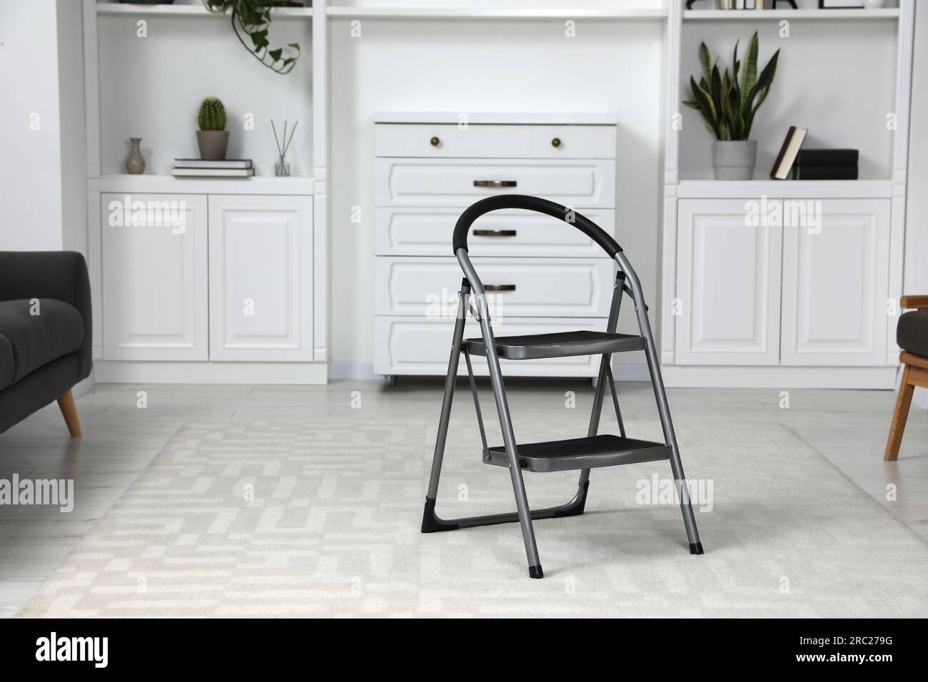 Metal folding ladder near chest of drawers and shelves with accessories ...