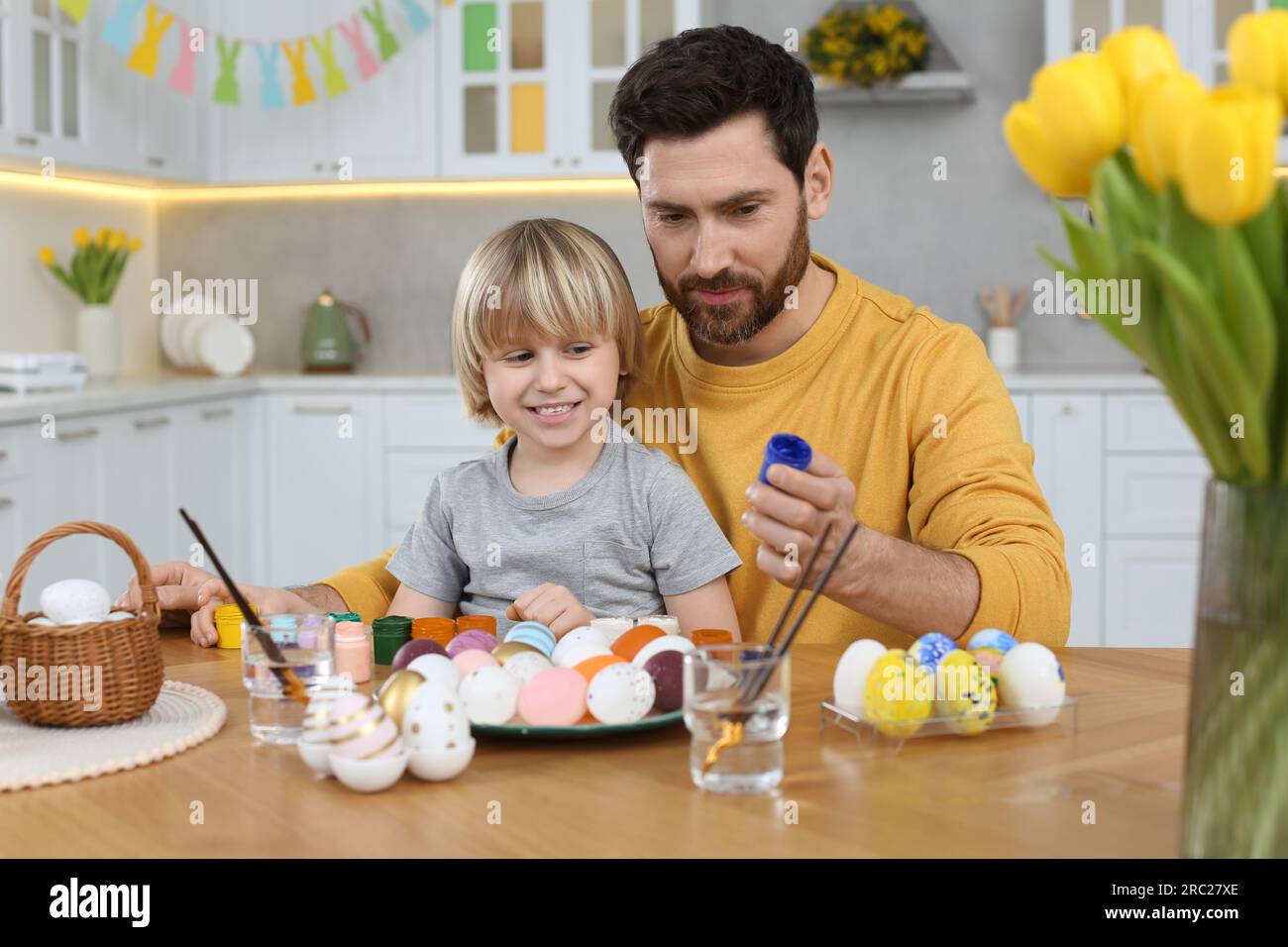 Father and his cute son painting Easter eggs at table in kitchen Stock ...