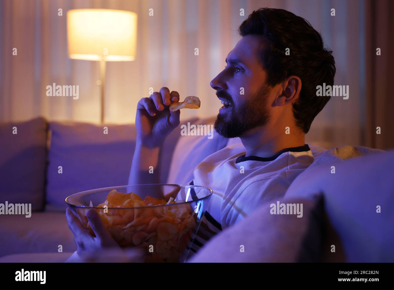 Man eating chips while watching TV on sofa at night. Bad habit Stock ...