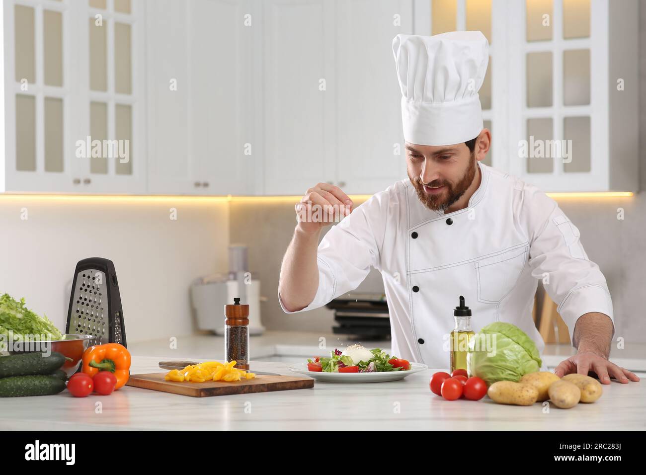 Professional chef salting delicious salad at marble table in kitchen ...