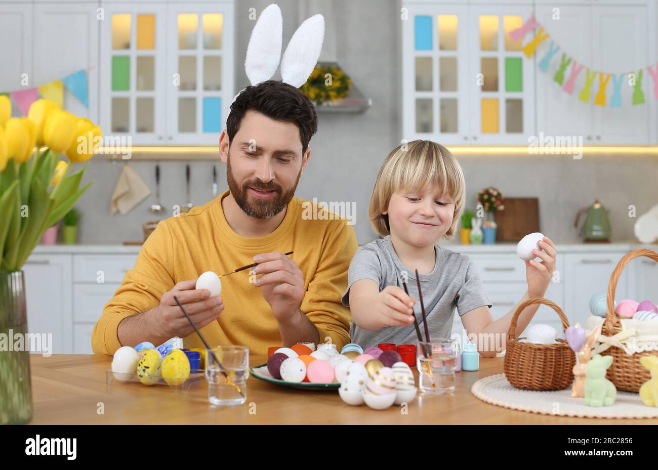 Father and his cute son painting Easter eggs at table in kitchen Stock ...