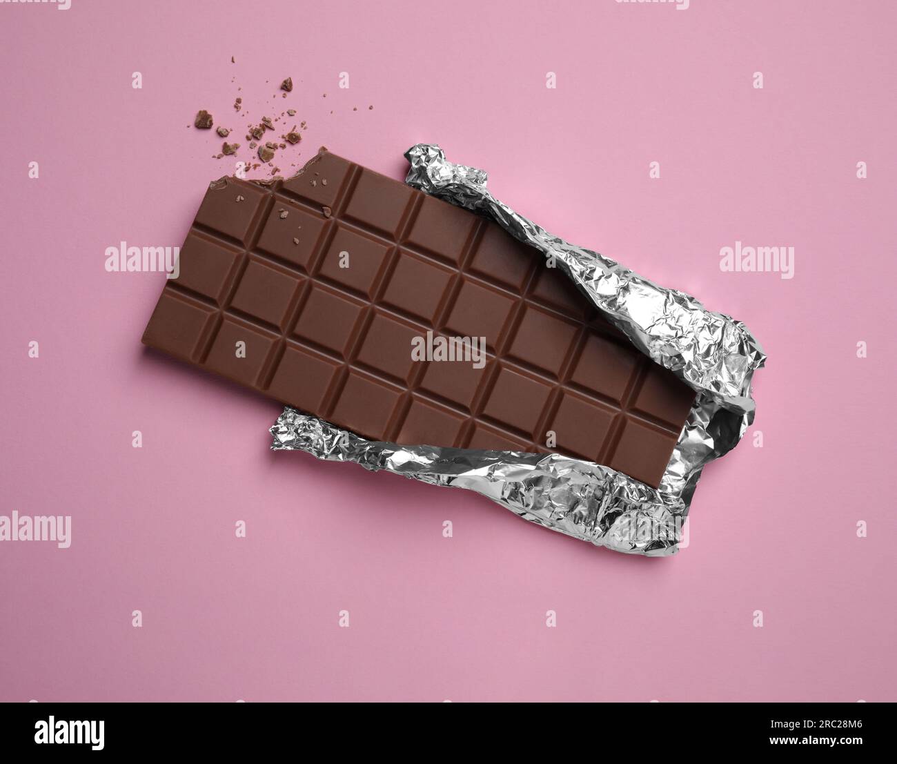 Bitten milk chocolate bar wrapped in foil on pink background, top view ...