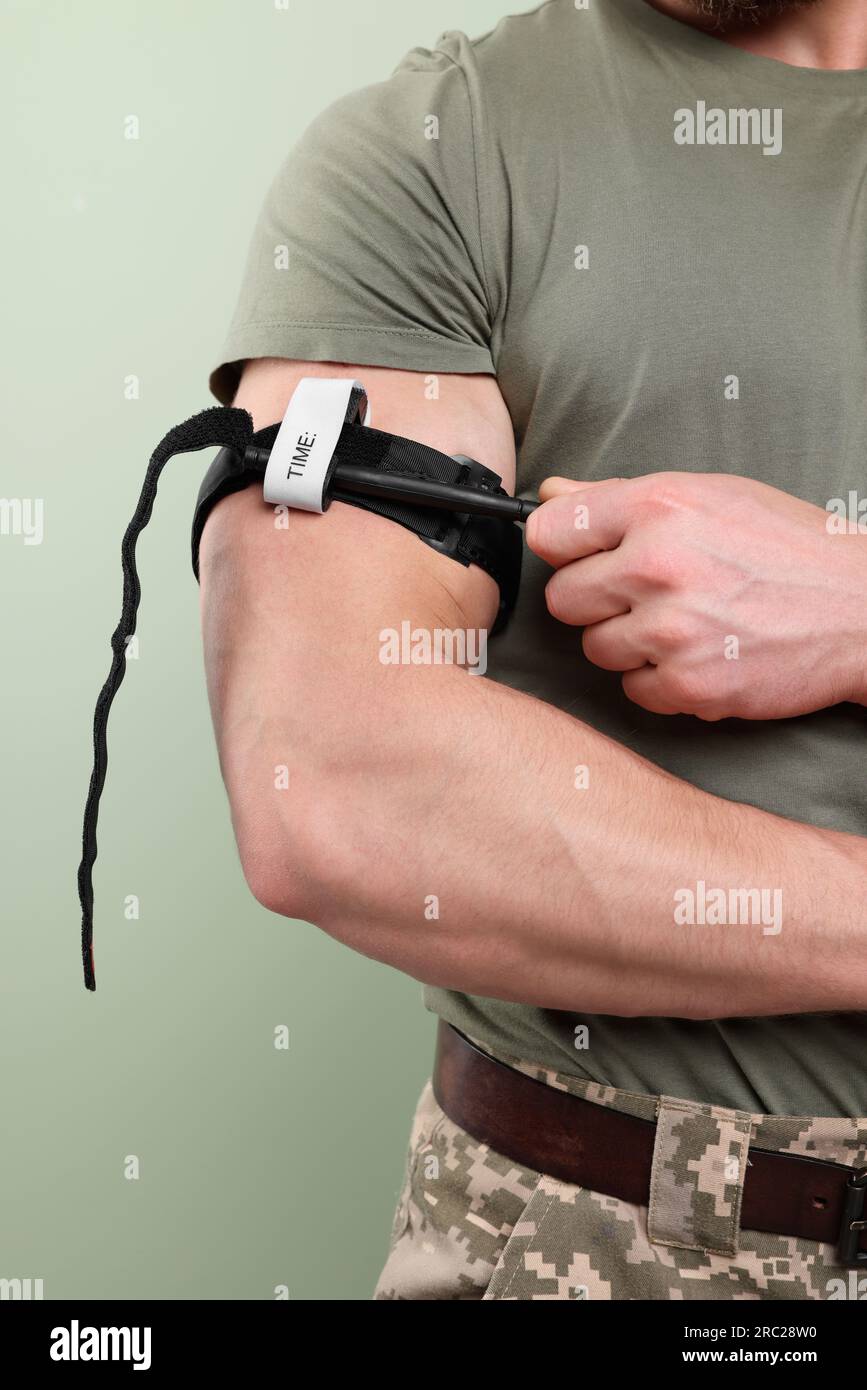 Soldier in military uniform applying medical tourniquet on arm against ...