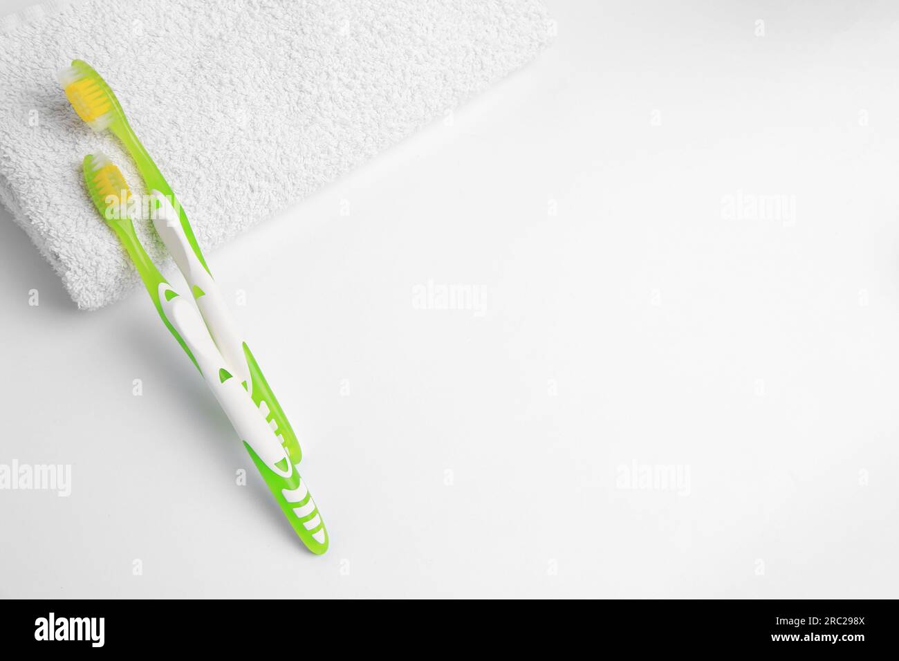 Light green toothbrushes and terry towel on white background, top view ...