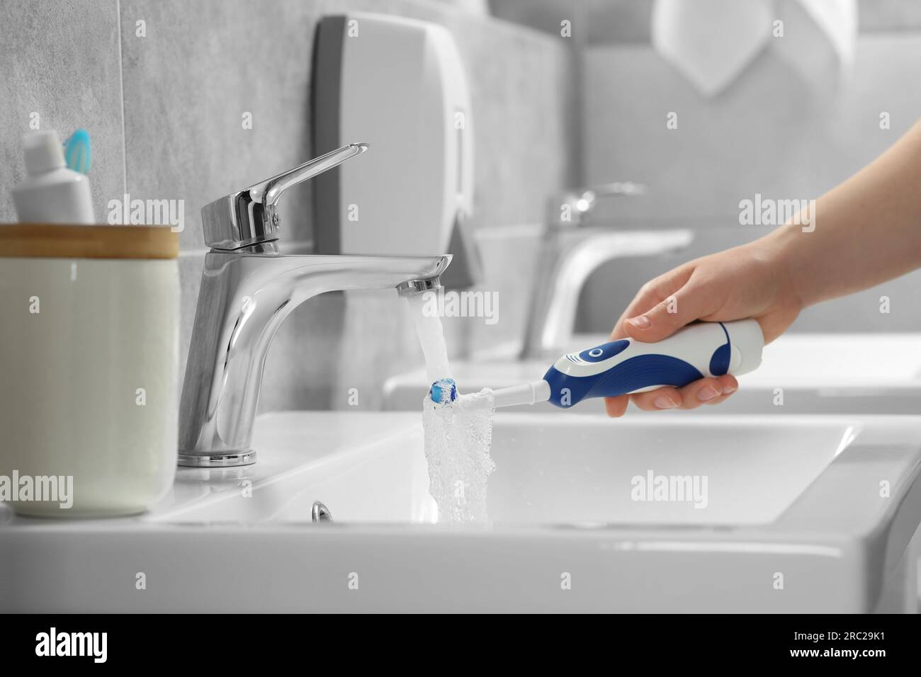 Woman washing electric toothbrush under flowing water from faucet in ...