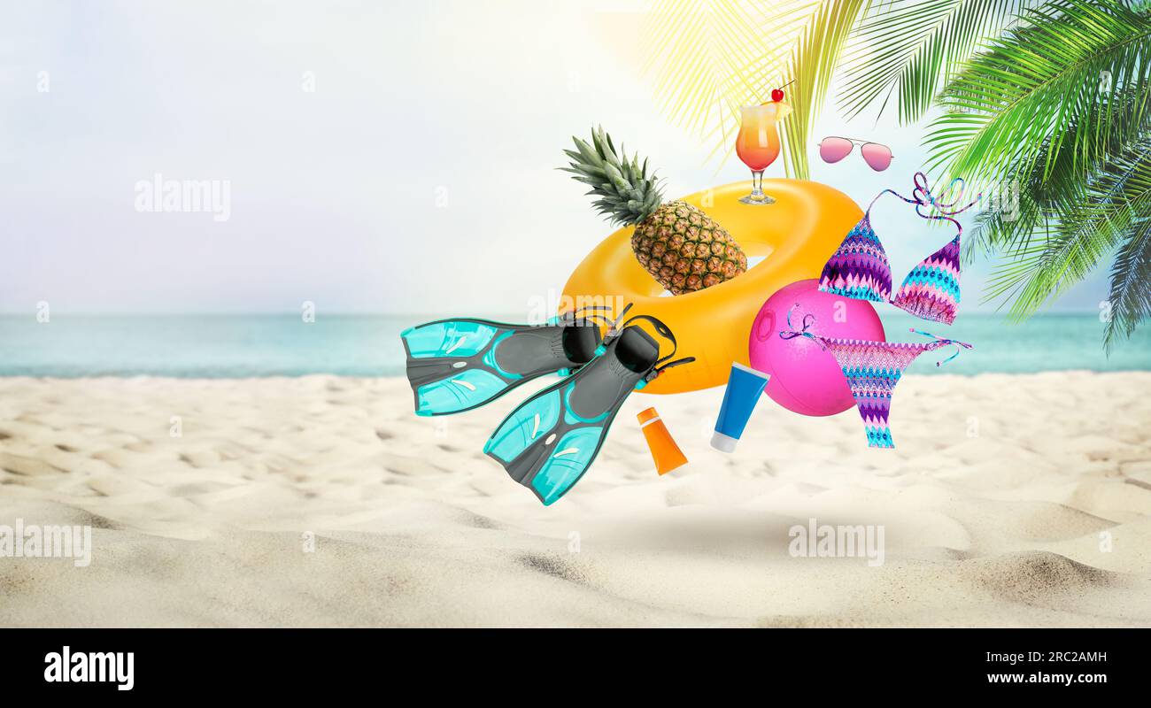 Pineapple, cocktail and beach accessories flying over sandy beach ...