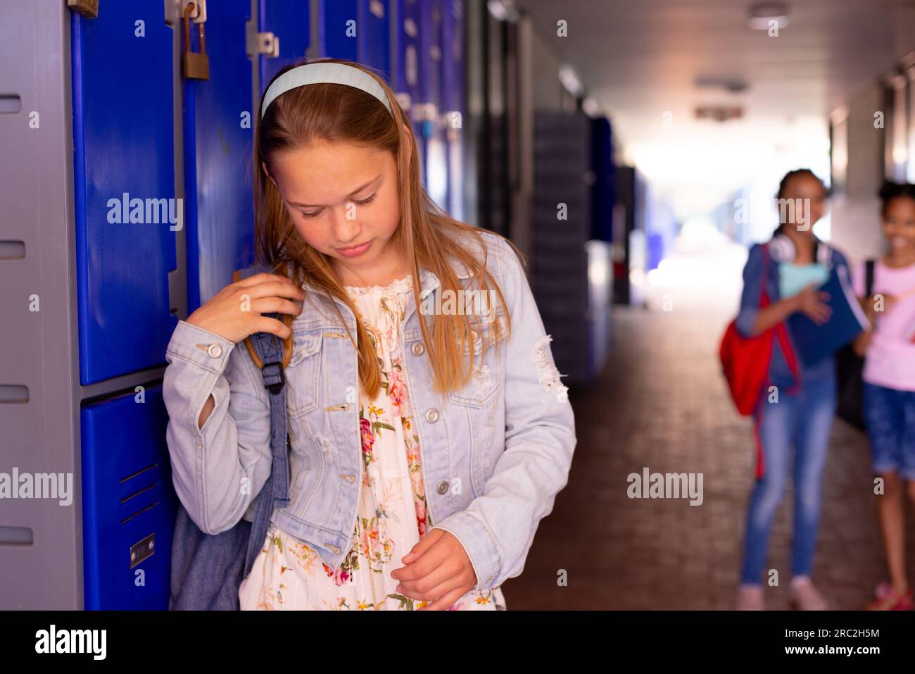 Sad caucasian schoolgirl standing next to lockers with diverse ...