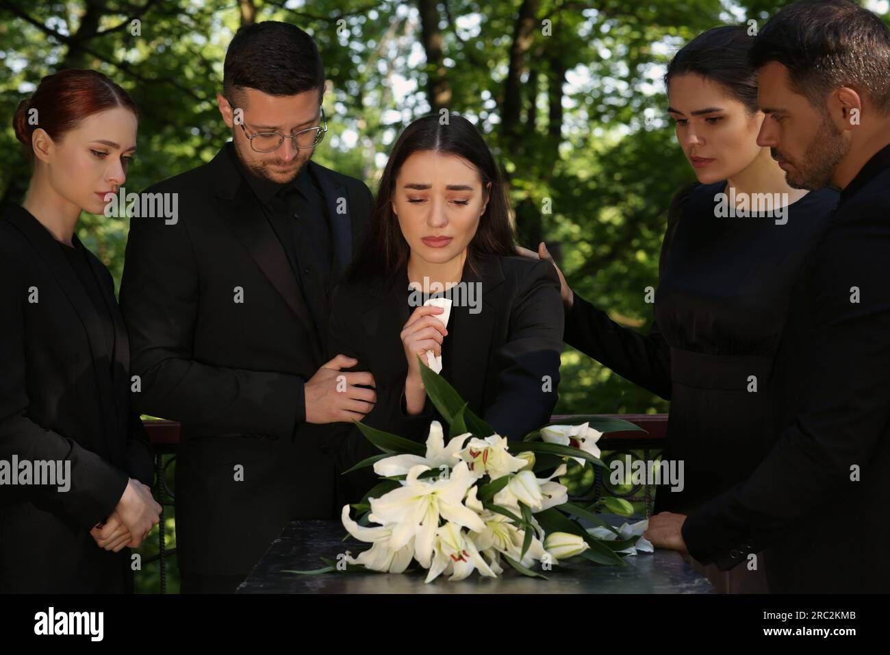 Funeral ceremony. Sad people mourning near granite tombstone with white ...