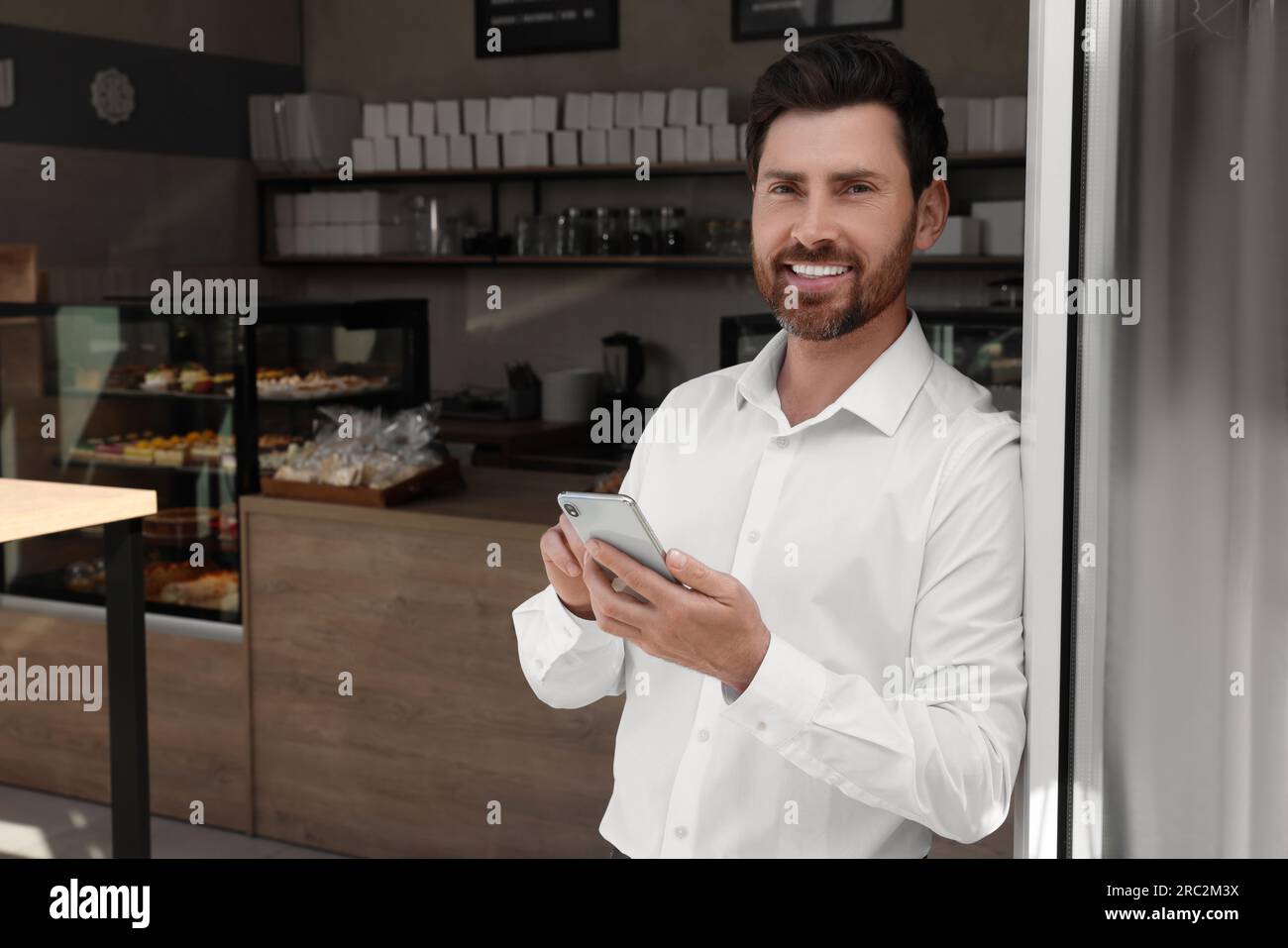 Happy business owner with smartphone in bakery shop. Space for text ...