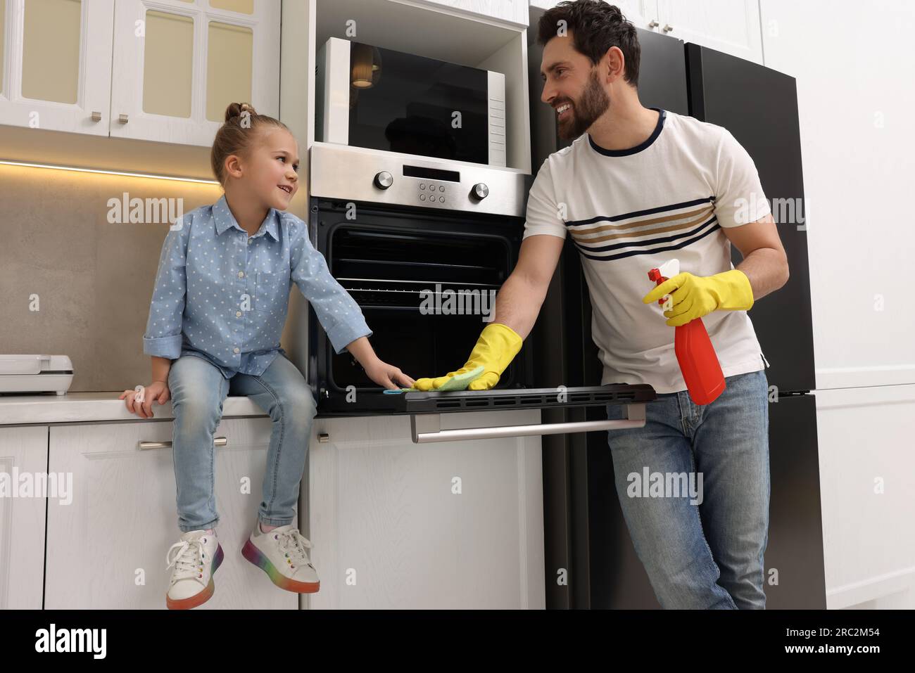 Spring cleaning. Father and daughter tidying up oven in kitchen ...