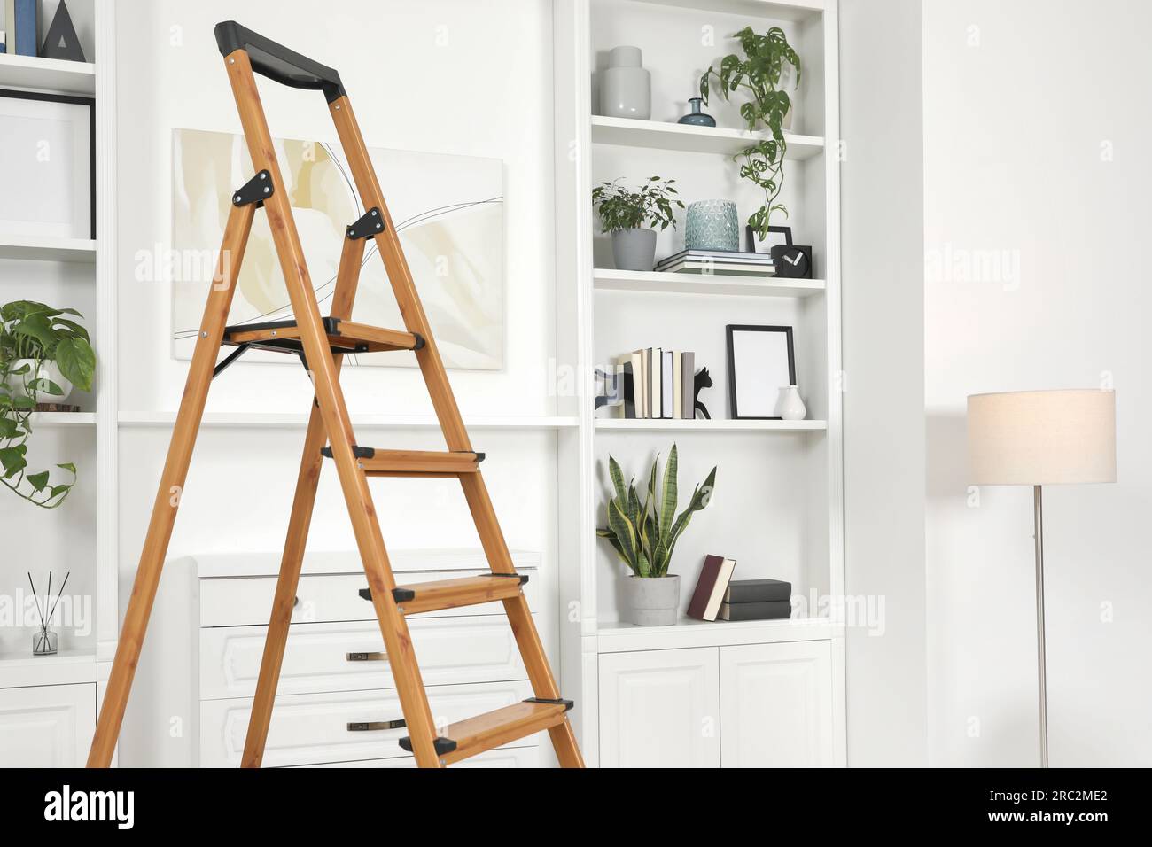 Wooden folding ladder near chest of drawers and shelves with ...