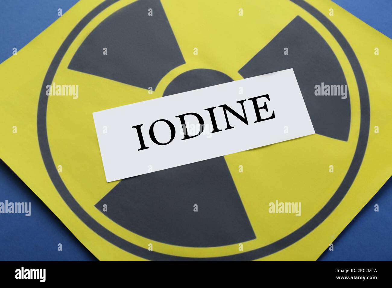 Paper note with word Iodine and radiation sign on blue background ...