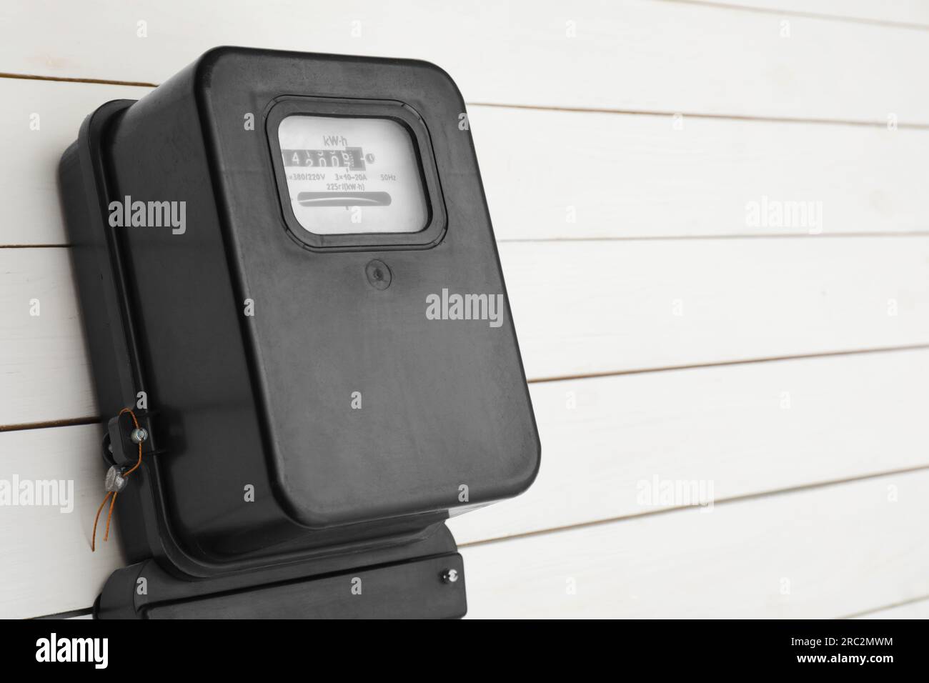 Black electric meter on white wooden wall, space for text. Measuring ...