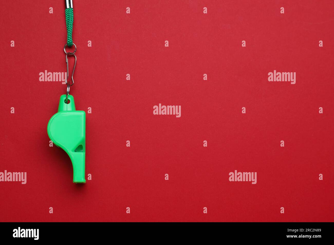 One green whistle with cord on red background, top view. Space for text ...