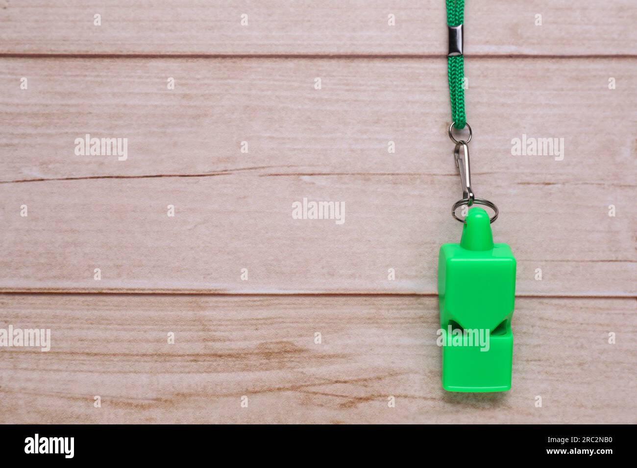 One green whistle with cord on light wooden table, top view. Space for ...