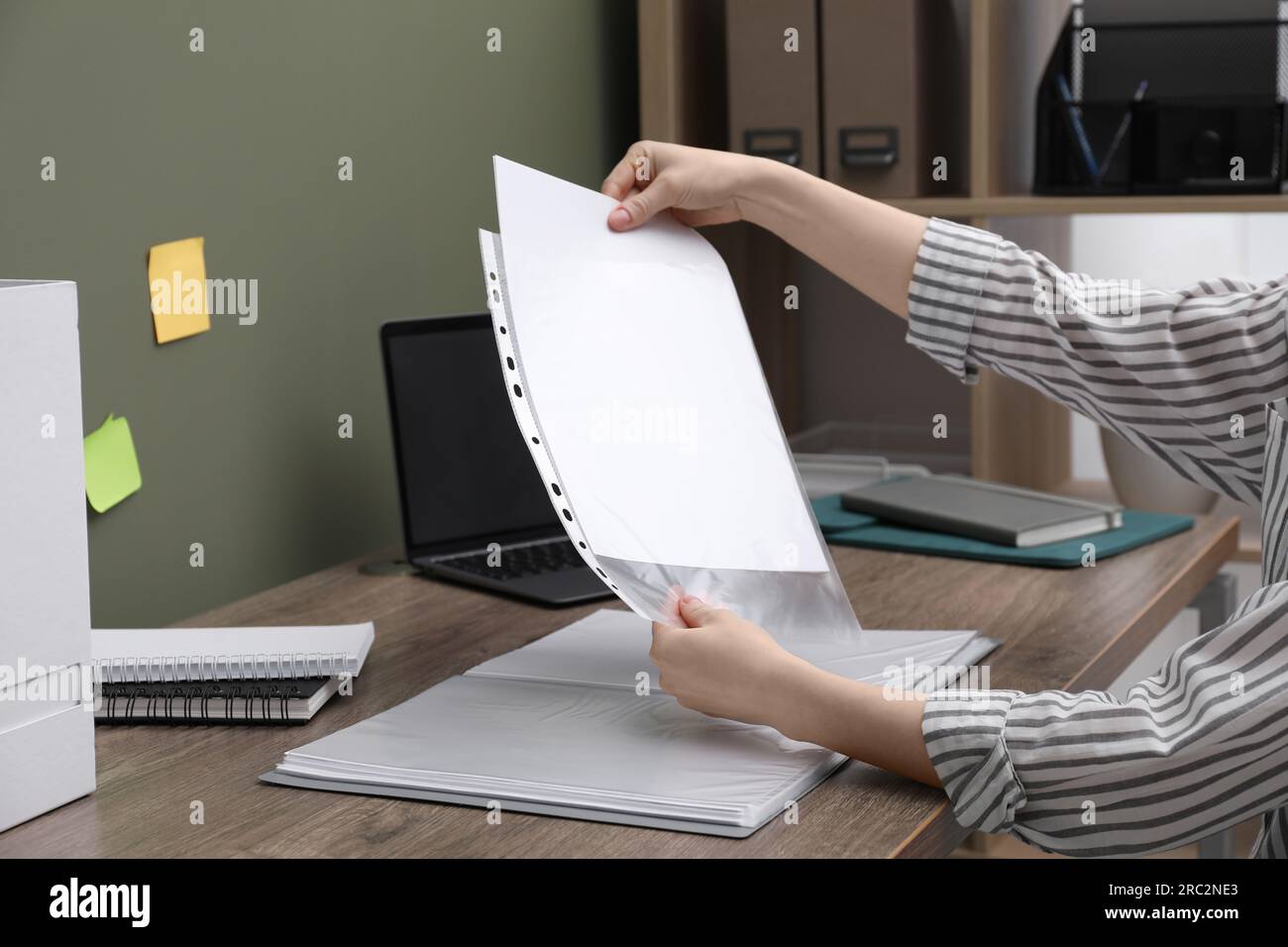 Woman putting paper sheet into punched pocket at wooden table, closeup ...