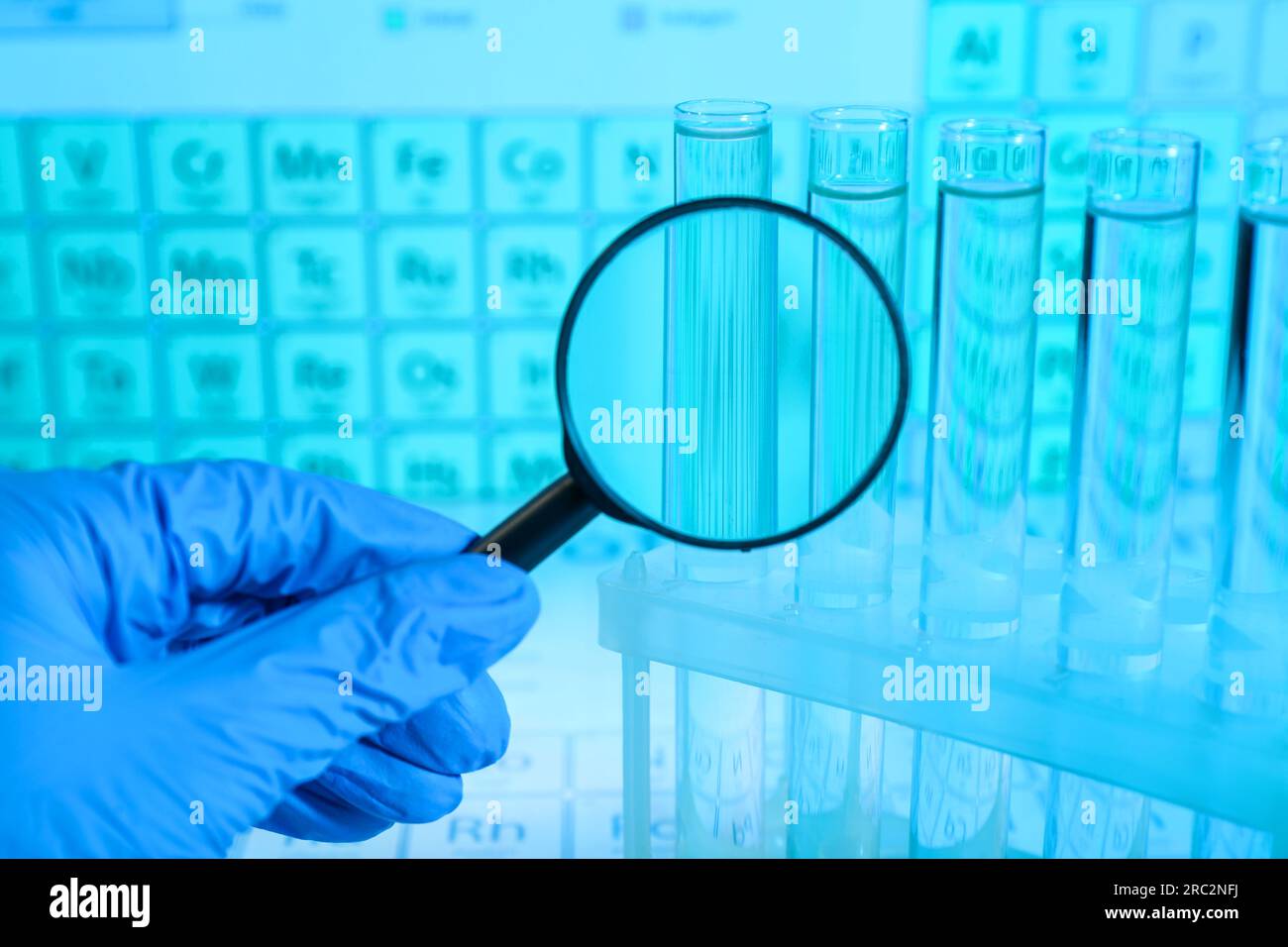 Scientist with magnifying glass examining test tubes against periodic ...