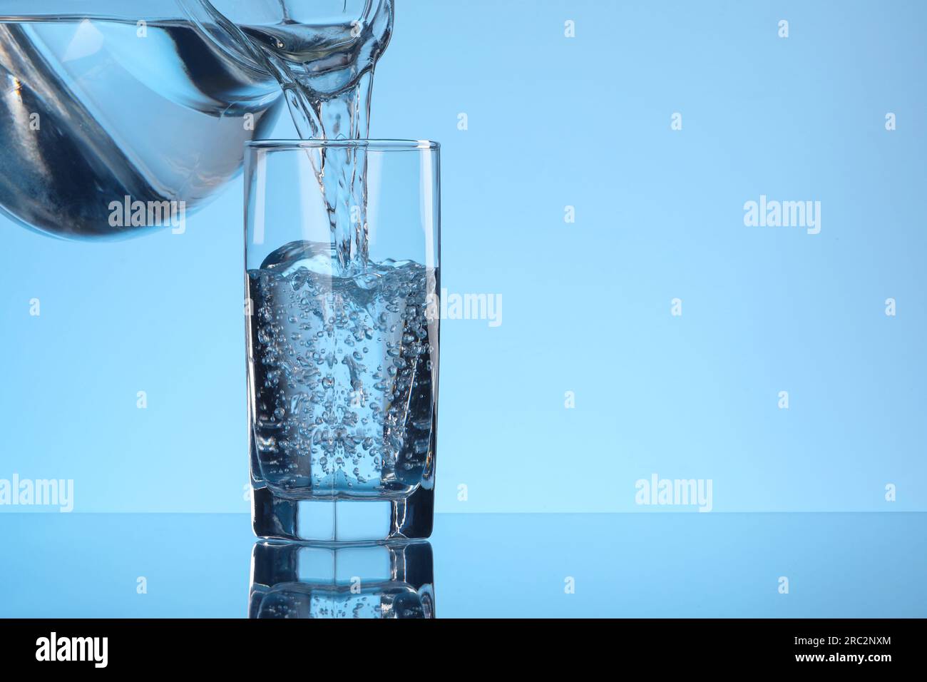 Pouring water from jug into glass on light blue background. Space for ...