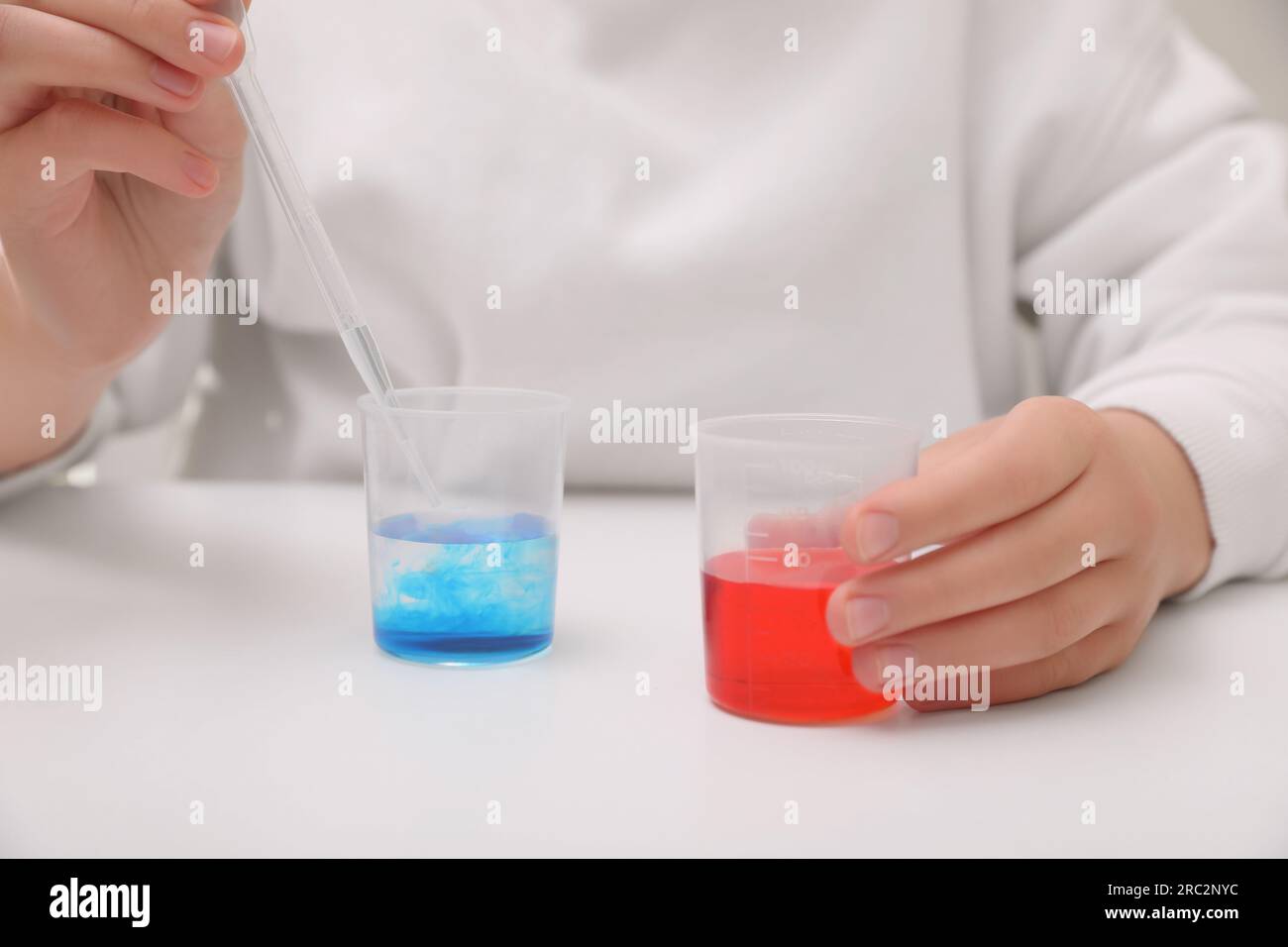 Girl mixing colorful liquids at white table indoors, closeup. Chemical ...