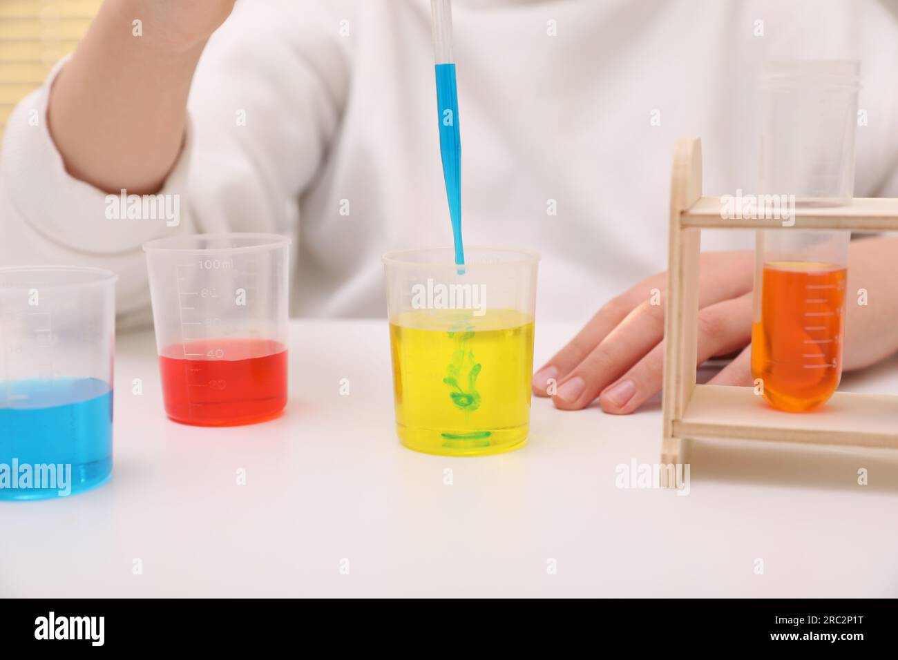 Girl mixing colorful liquids at white table indoors, closeup. Chemical ...