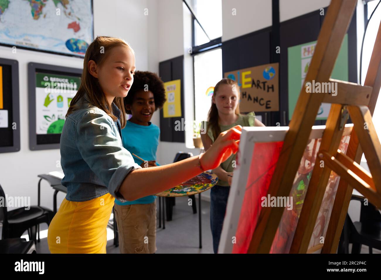 Happy diverse schoolchildren painting using brush and easel in school ...
