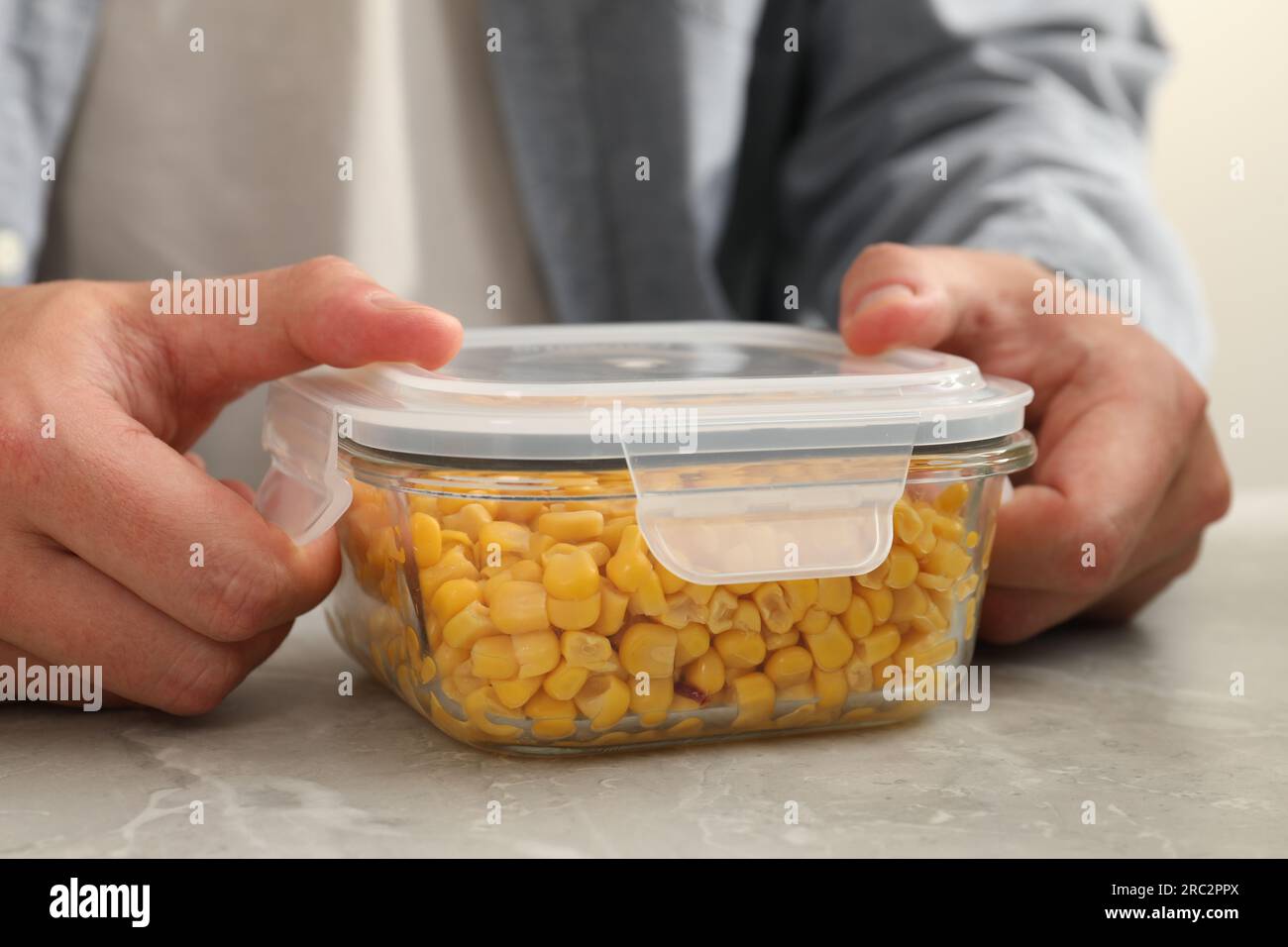 Man closing glass container with lid at light grey marble table in ...