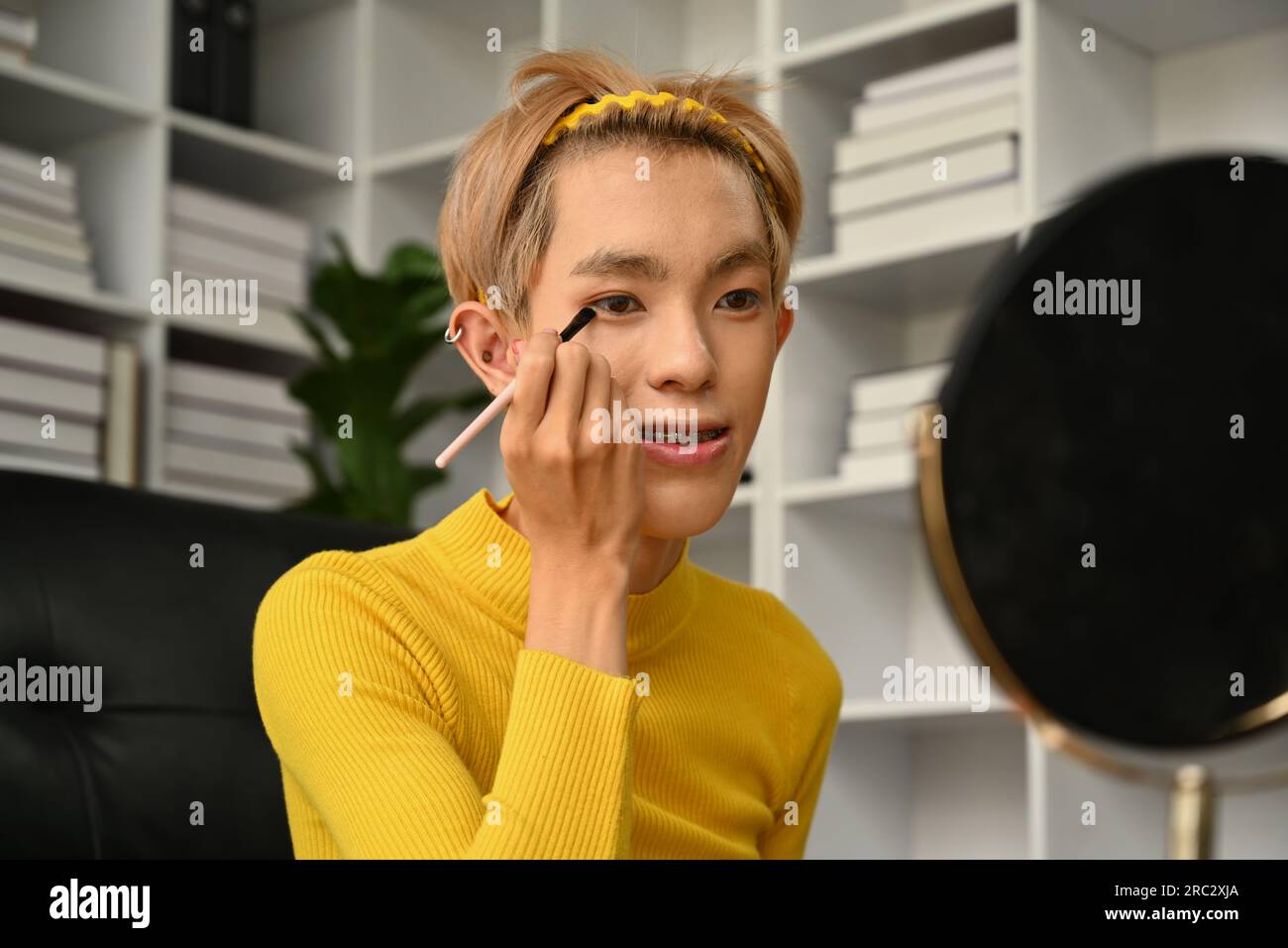 Teenage asian man applying eyeshadow powder in front of mirror with ...