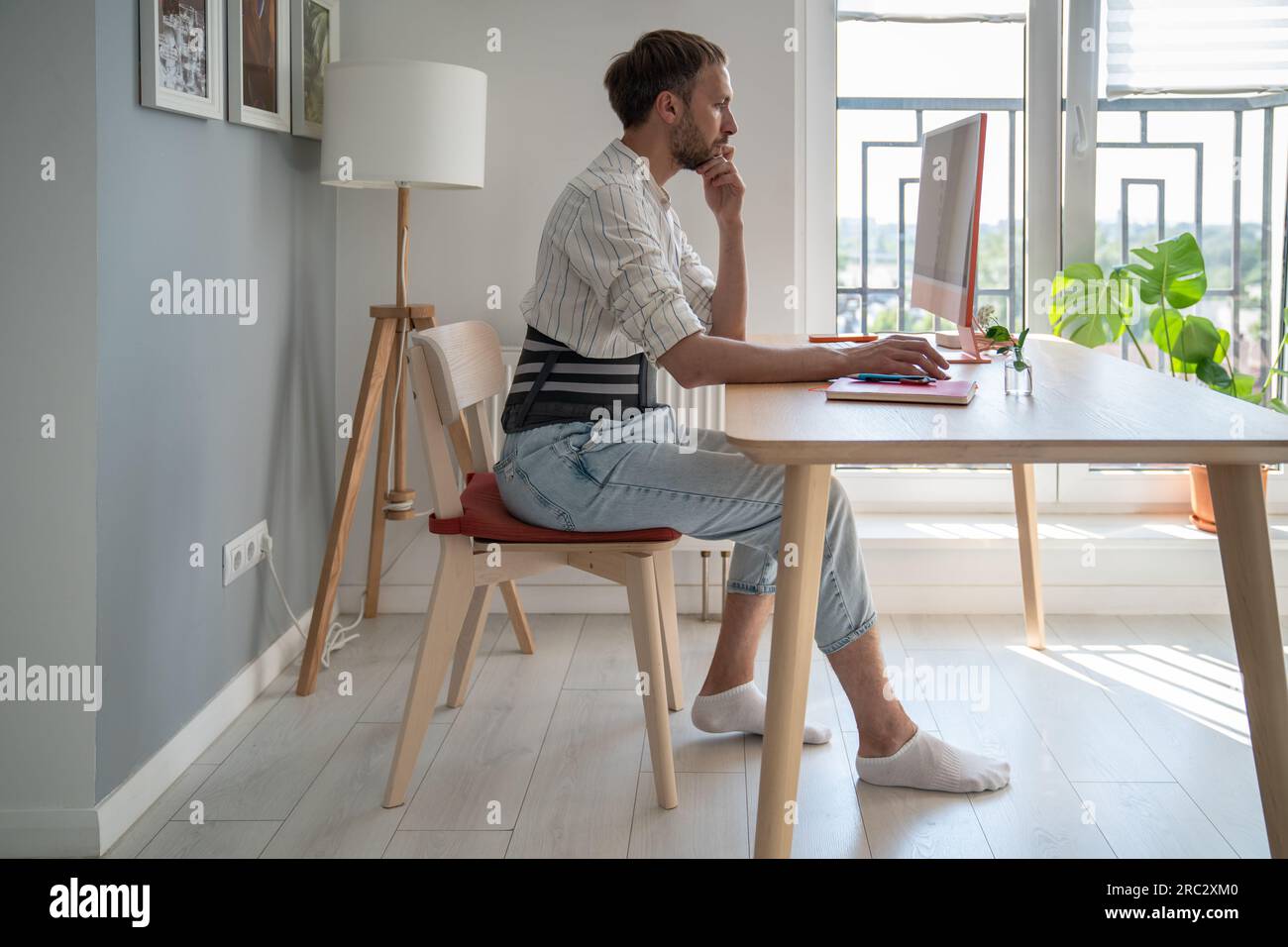 Young man freelancer wearing back brace sitting at table using computer ...