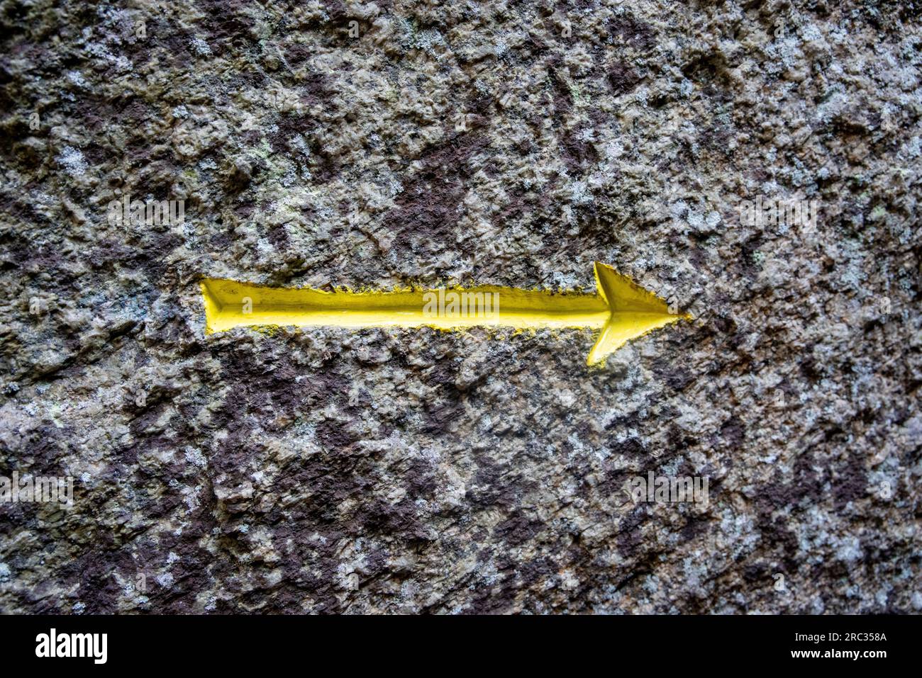 mountain pointer on yellow arrow on a stone close-up, direction forward ...