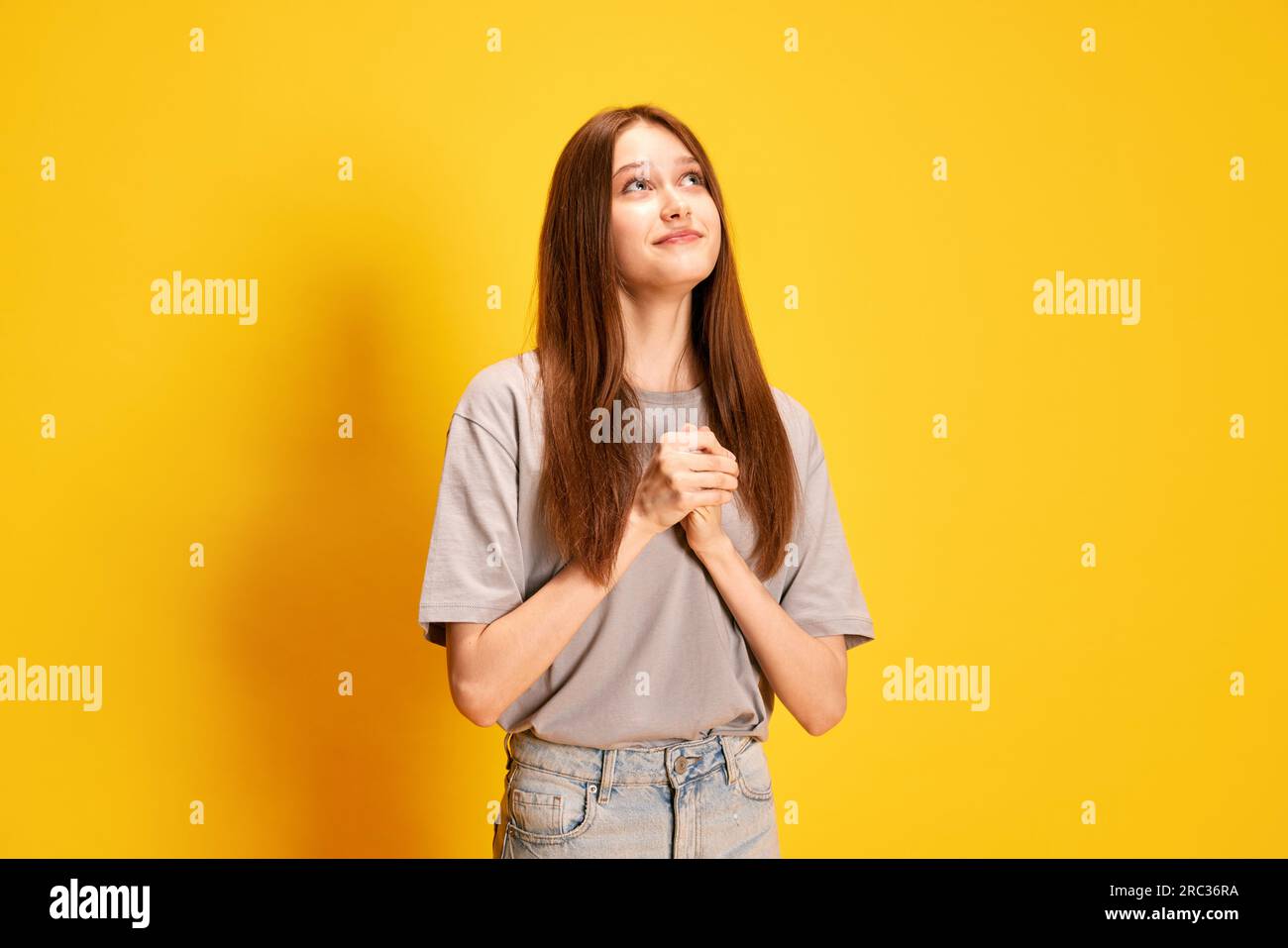 Portrait of young pretty girl with dreamy face against yellow studio ...