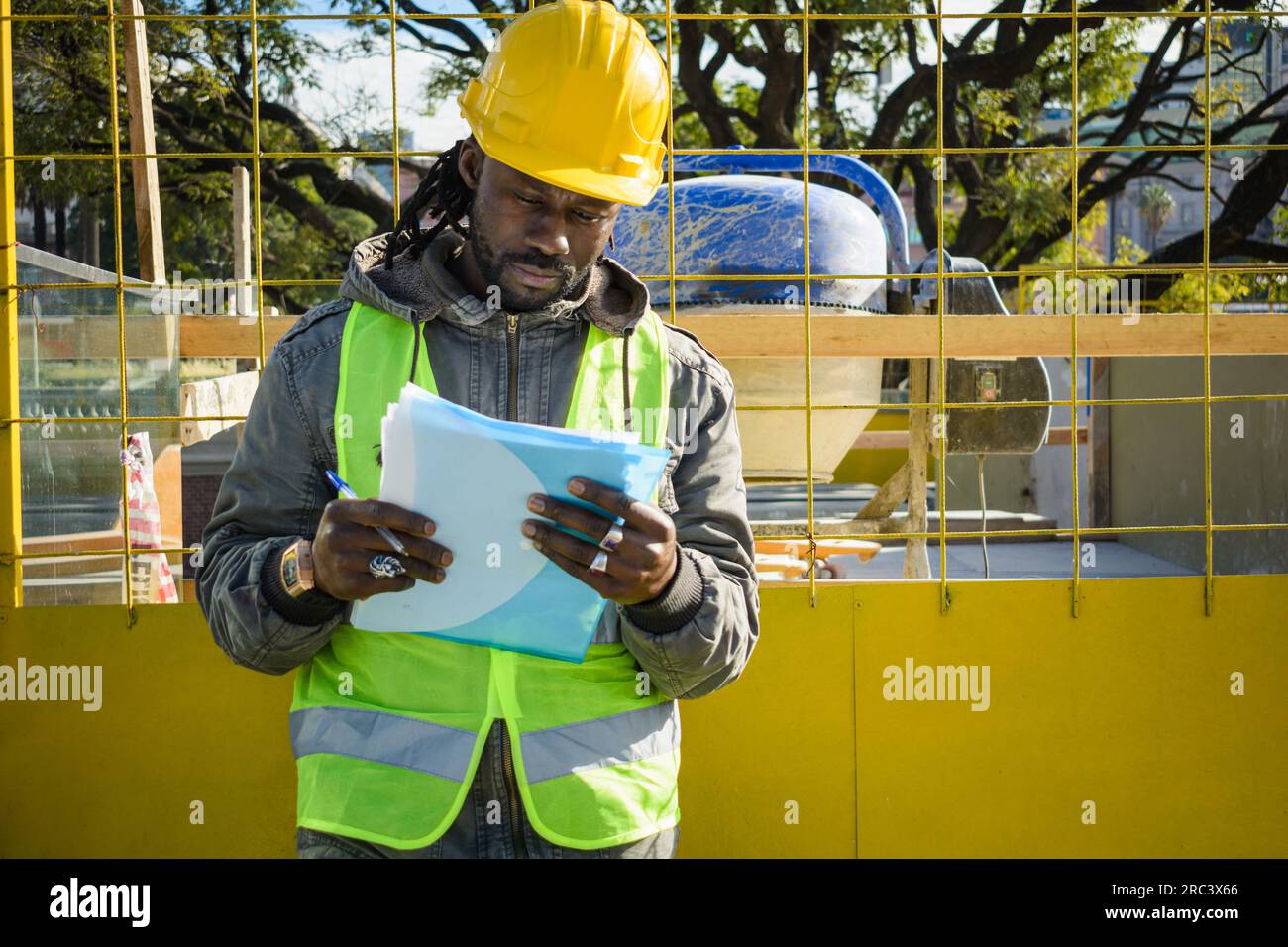 black ethnic male civil engineer wearing yellow hardhat, green jacket ...