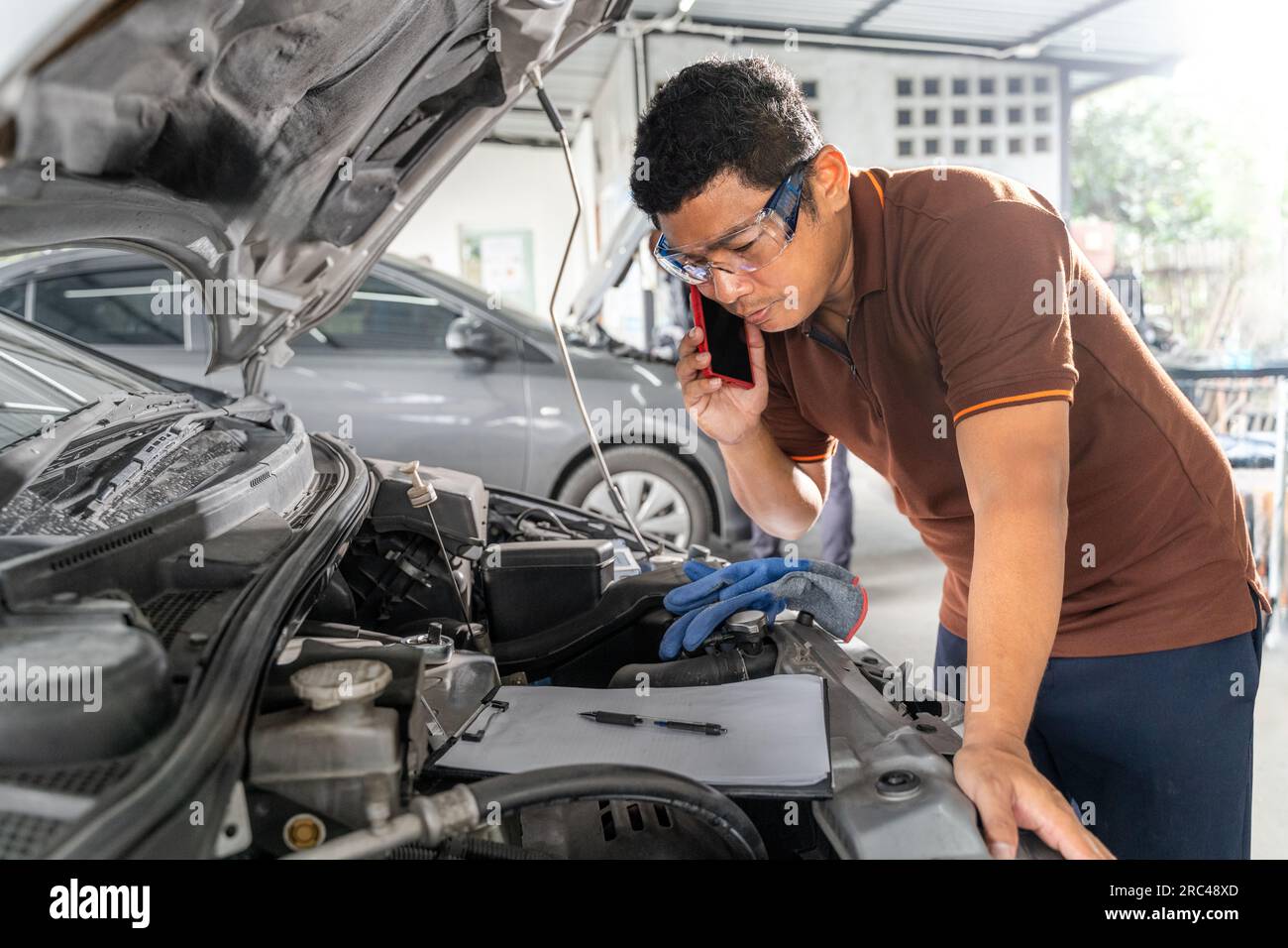 An Asian male car mechanic using his phone while working on repairing a ...