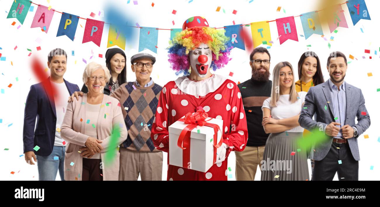 Clown holding a present at a birthday party with people gathered behind ...