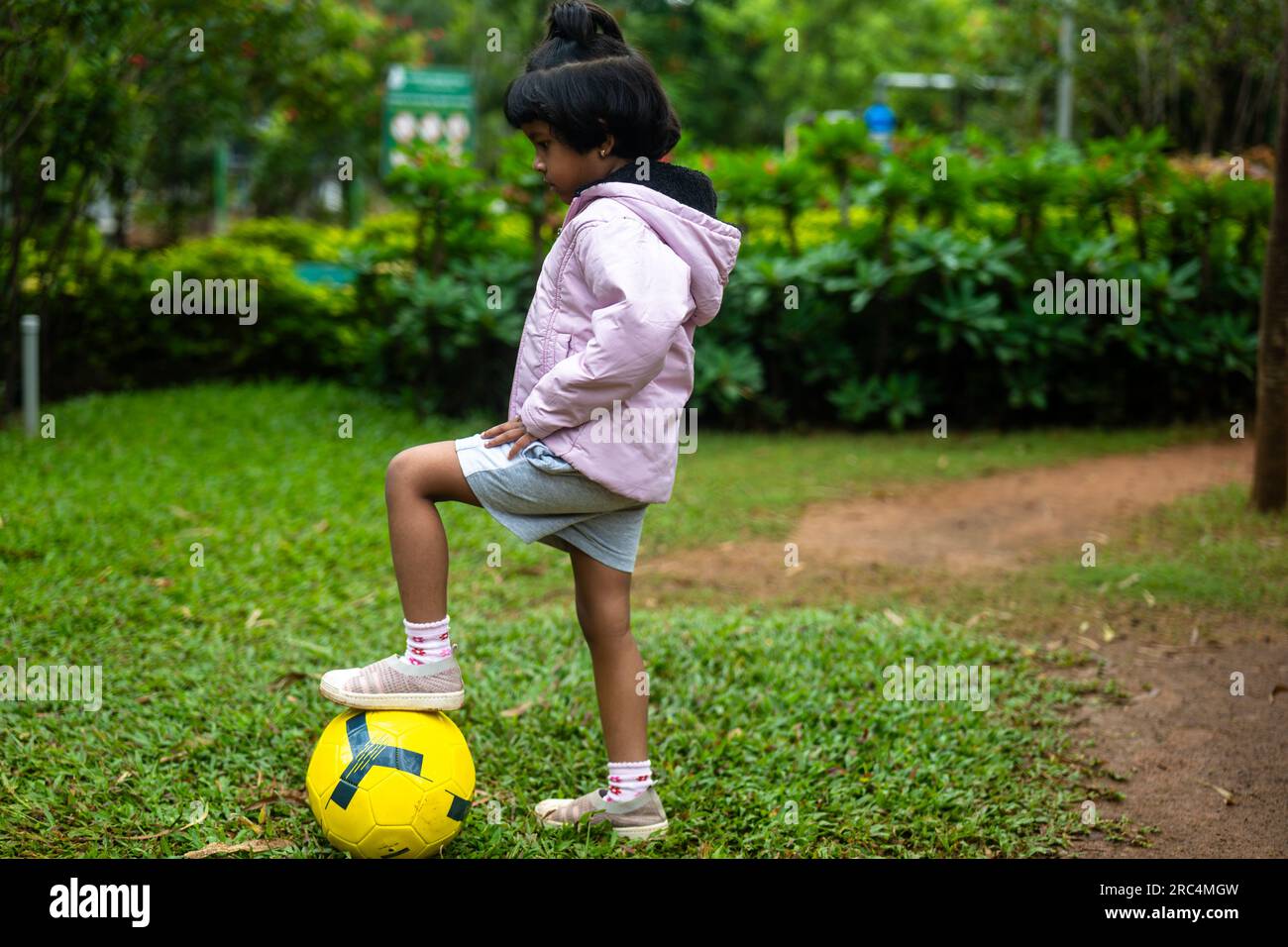 A young girl in a soccer uniform is holding a football in her leg ...