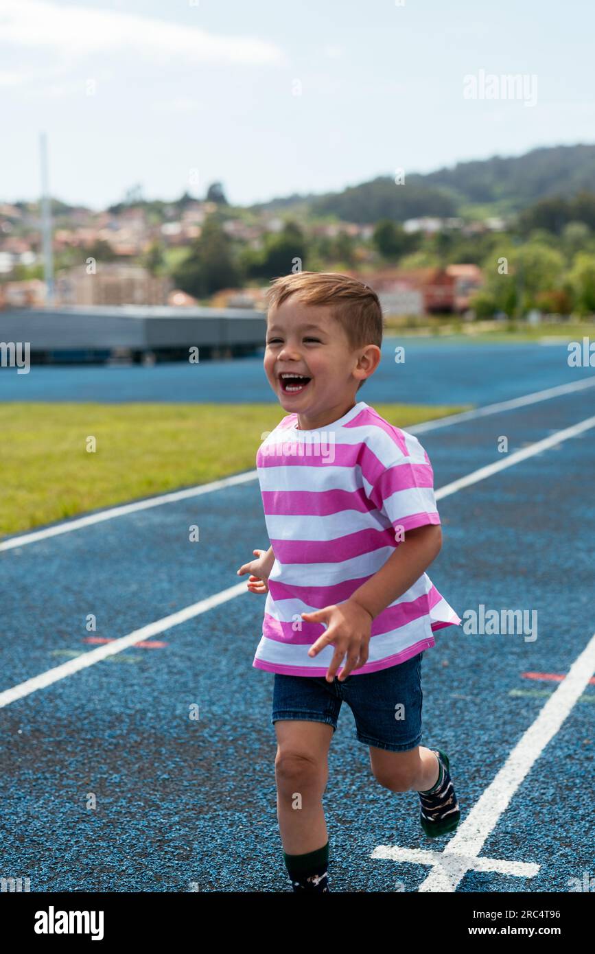 Cheerful adorable little boy in casual clothes running along racetrack ...
