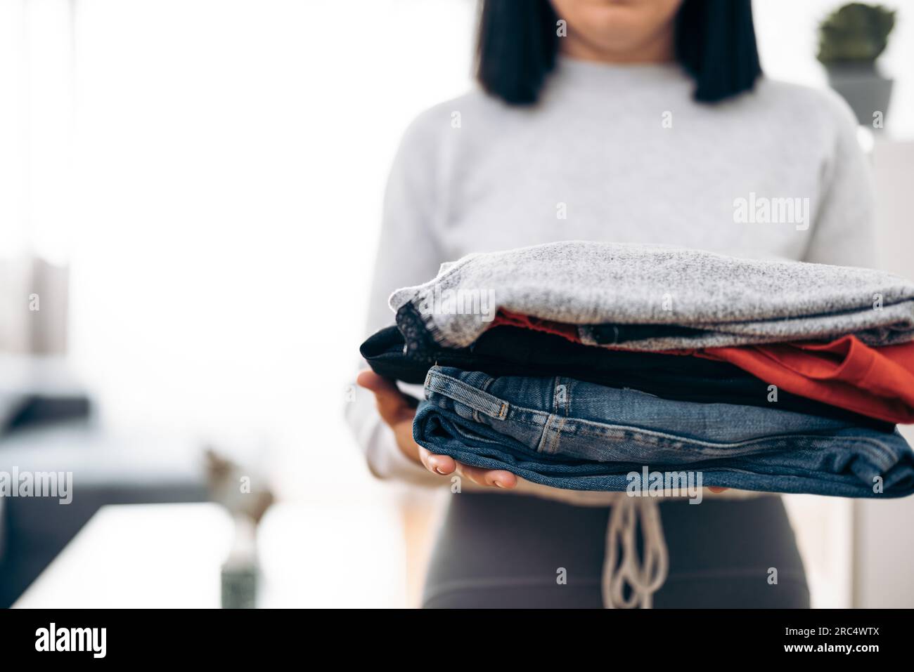 Front view of unrecognizable woman carrying folded clothes against ...