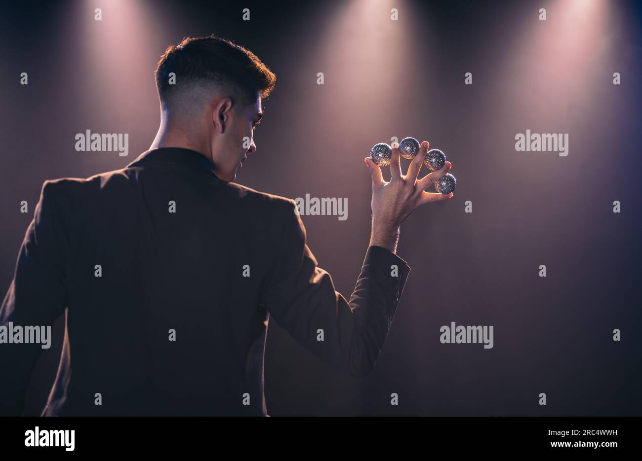 Back view of faceless male juggler in black suit with metal balls ...