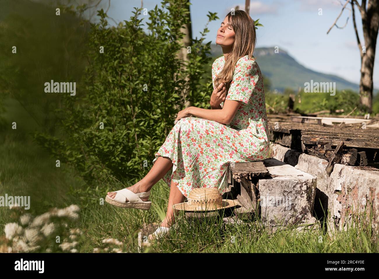 Full body of calm female in sundress sitting on stone step in green ...