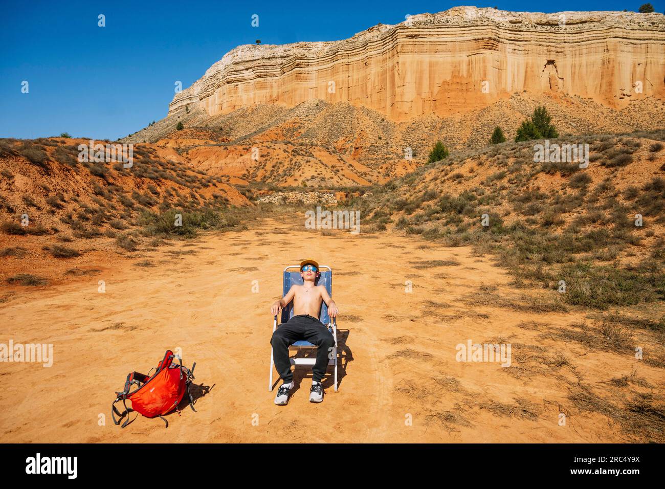 High angle of teen male camper in sunglasses sitting on foldable chair ...