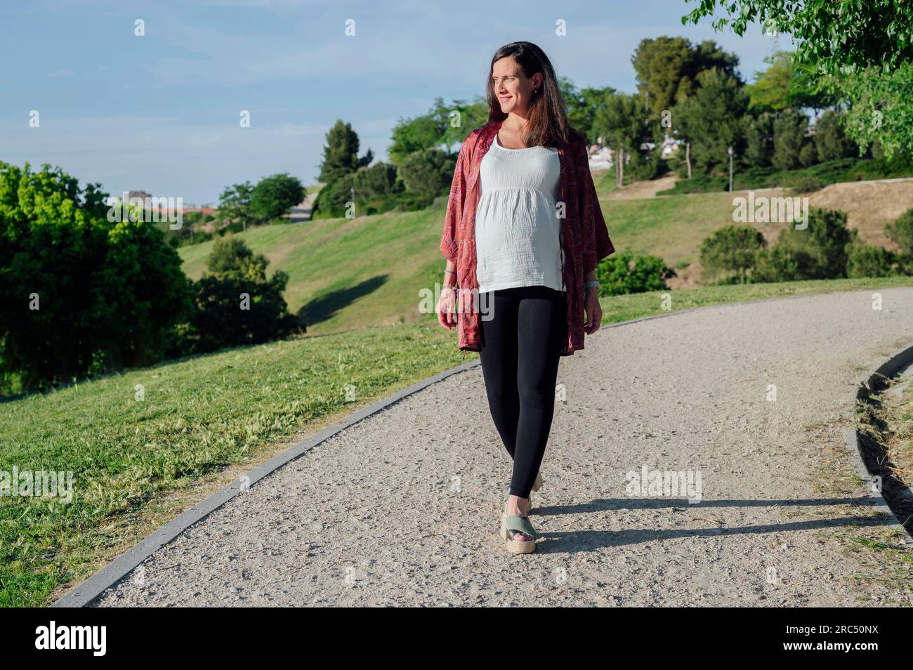 Full body of glad expecting female in maternity clothes smiling while ...