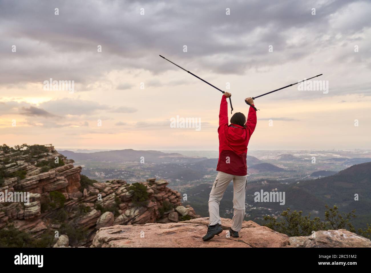 Back view of unrecognizable female traveler holding trekking poles with ...