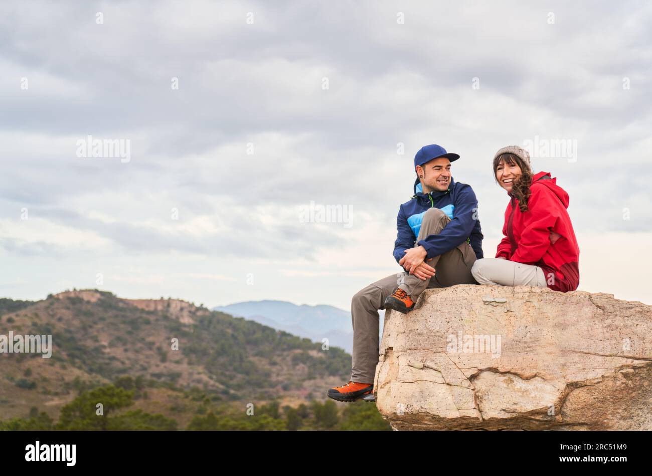 Cheerful wife and husband sittinf on edge on top of mountain enjoying ...