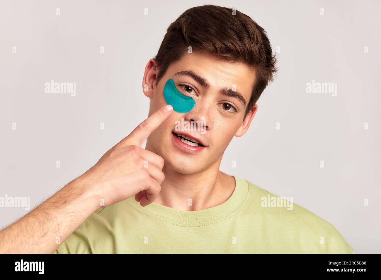 Young handsome smiling guy with brown hair applying under eye hydrogel ...