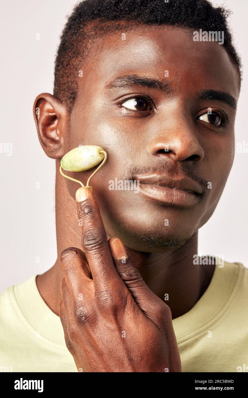 Young handsome black guy using jade de-puffing face roller to keep his ...