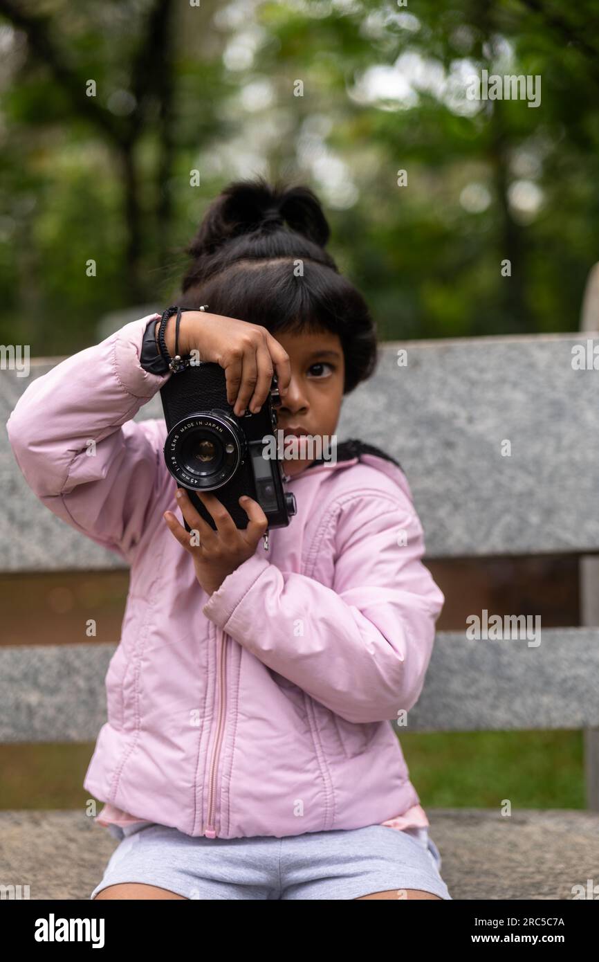 A young girl holds a DSLR camera and looks through the viewfinder ...