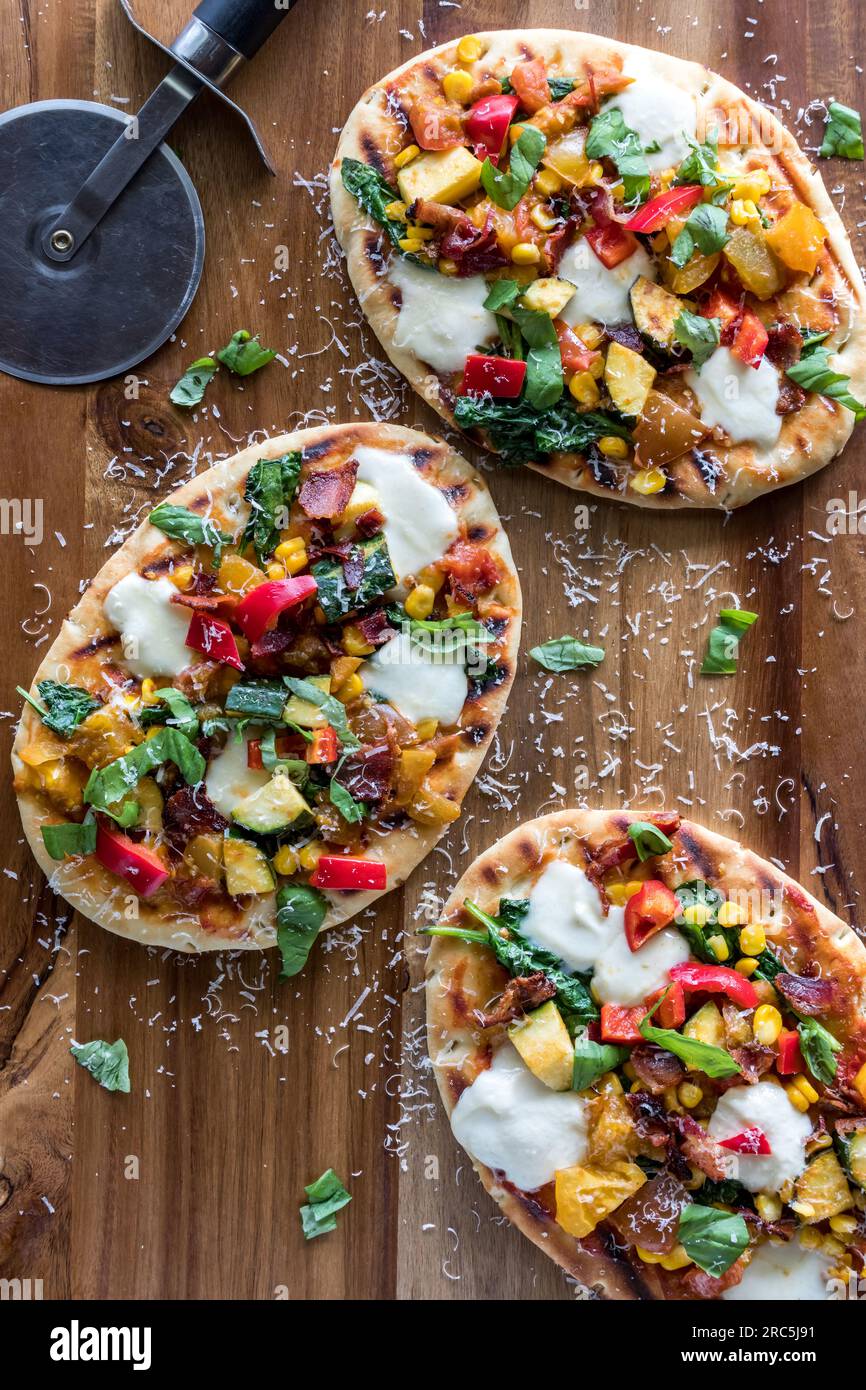 Three homemade summer garden pizzas on a wooden board, ready for eating ...